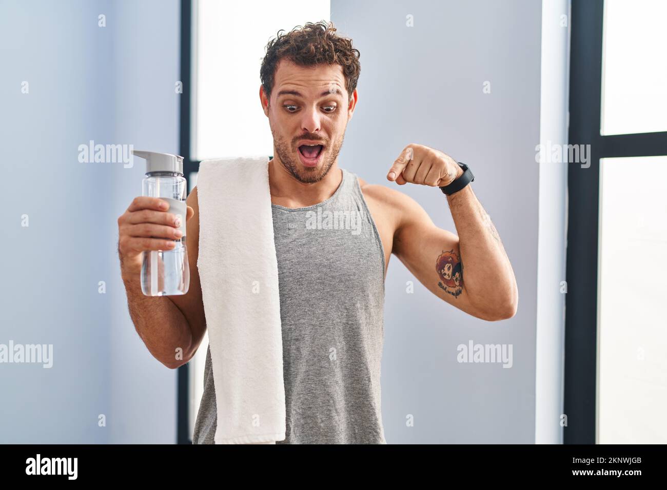 Young hispanic man wearing sportswear drinking water pointing down with ...