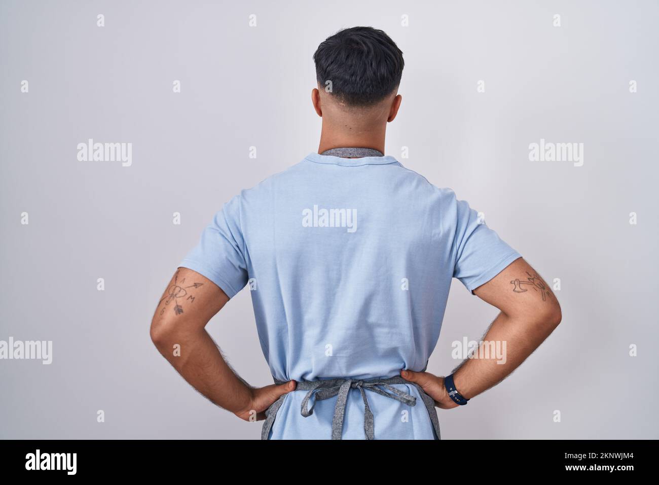 Hispanic young man wearing apron over white background standing ...