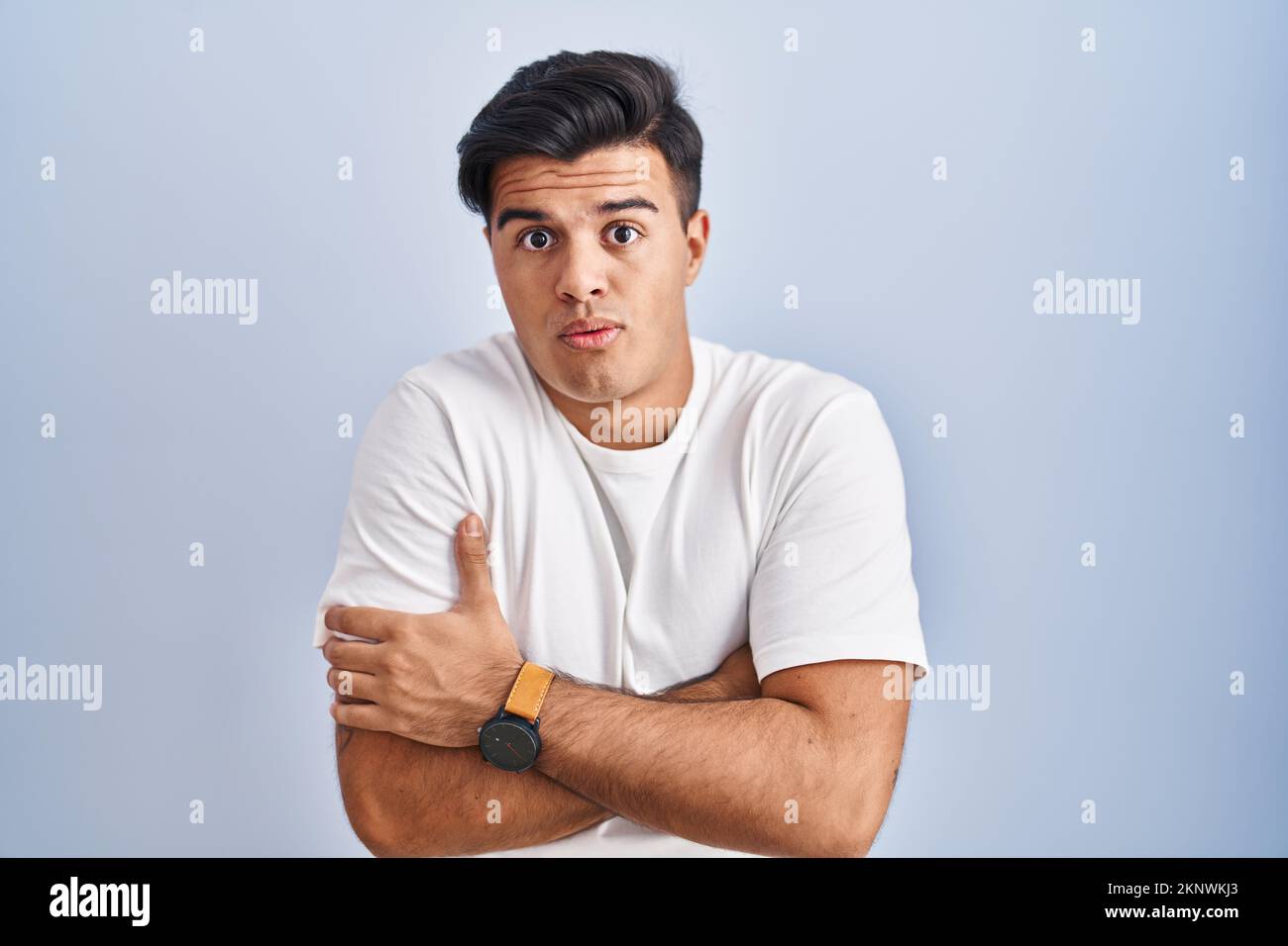 Hispanic man standing over blue background shaking and freezing for ...