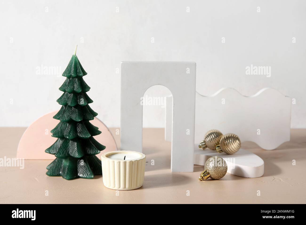 Christmas tree candle with podiums and balls on table near light wall ...