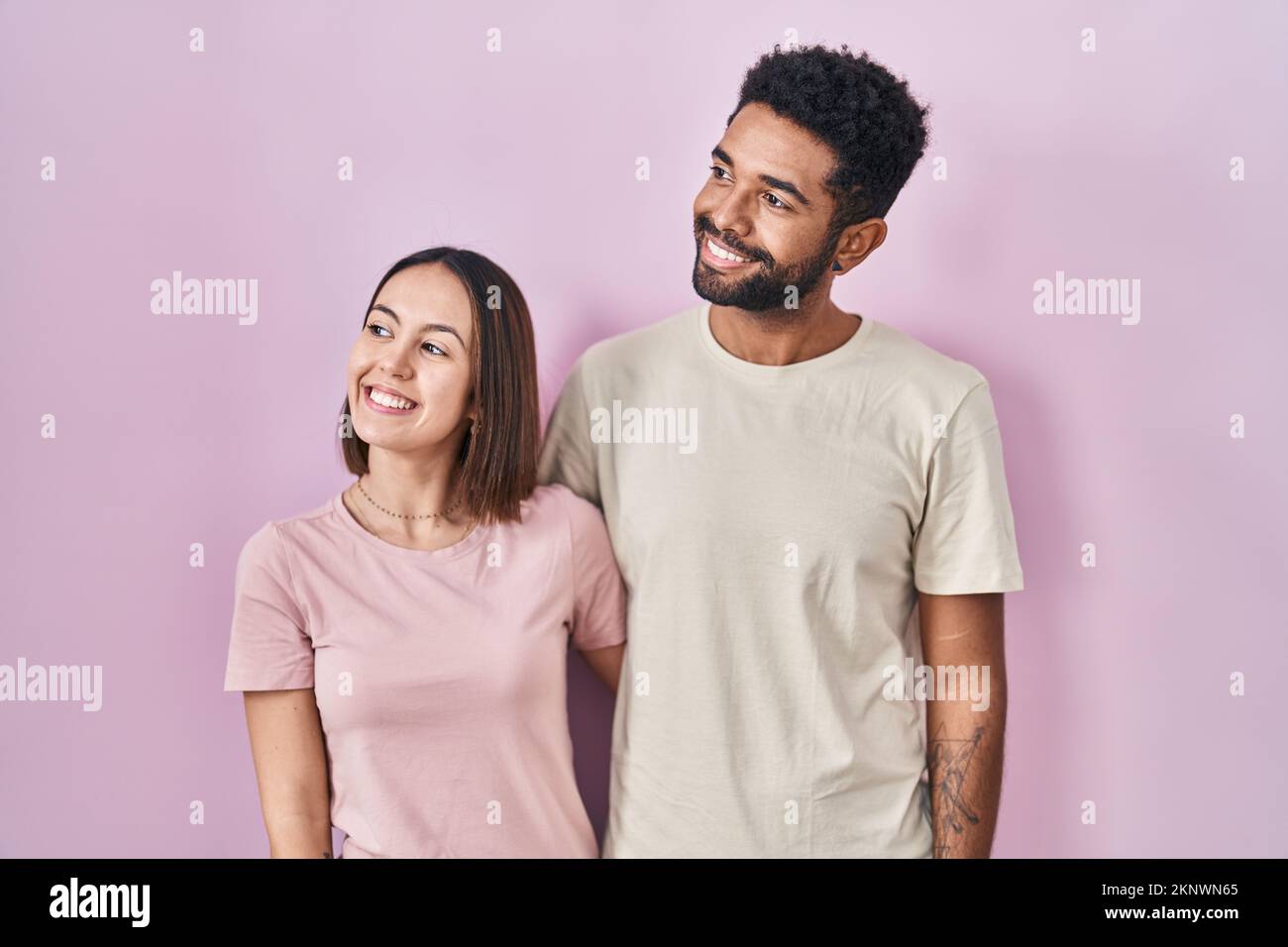 Young hispanic couple together over pink background looking away to ...