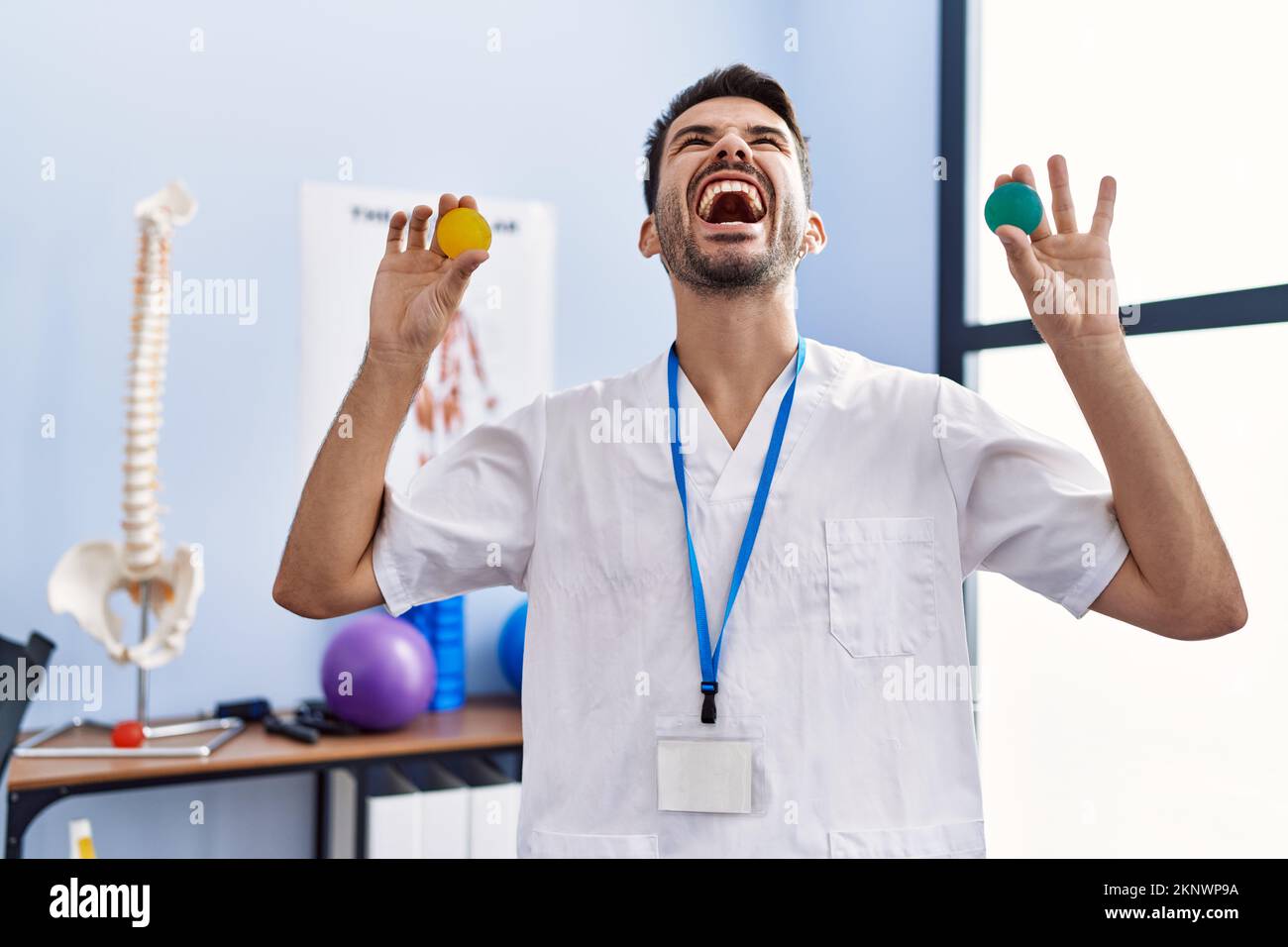 Young hispanic physiotherapist man holding strength balls to train hand ...