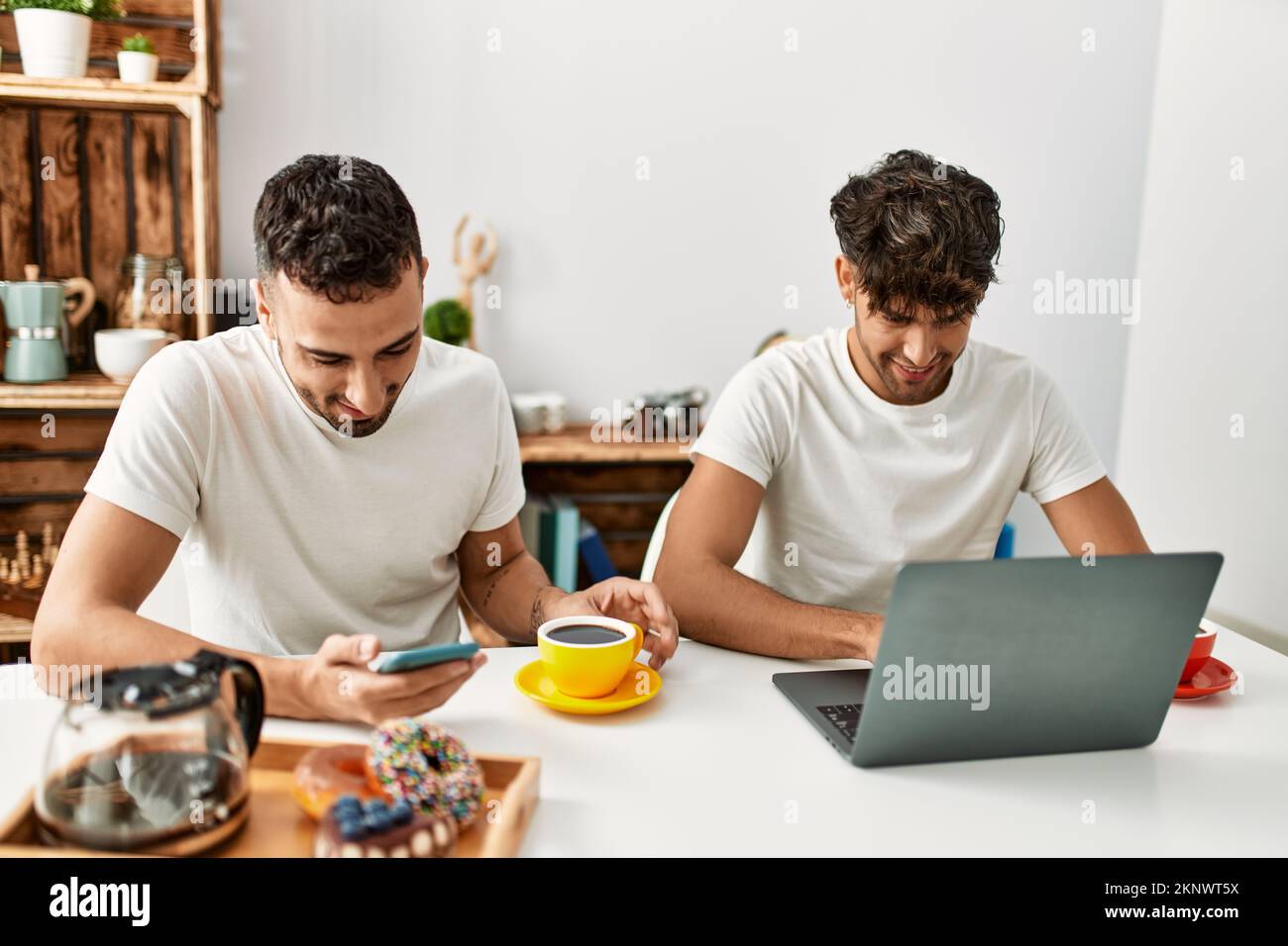 Two hispanic men couple having breakfast using smartphone and laptop at ...