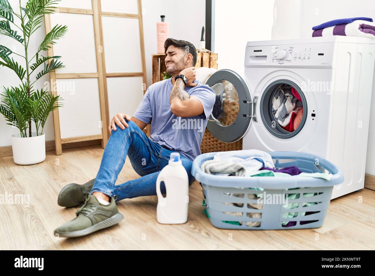 Young hispanic man putting dirty laundry into washing machine suffering ...