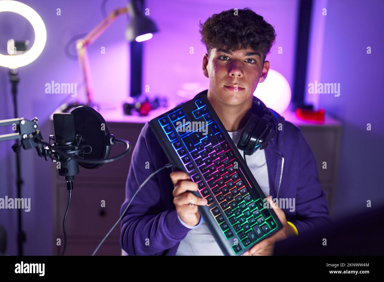 Young hispanic teenager streamer holding computer keyboard with relaxed ...