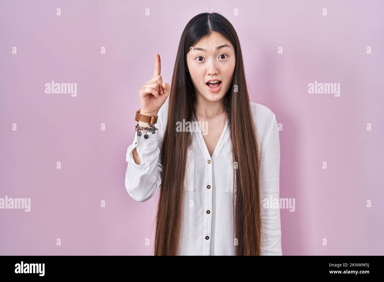 Chinese young woman standing over pink background pointing finger up ...