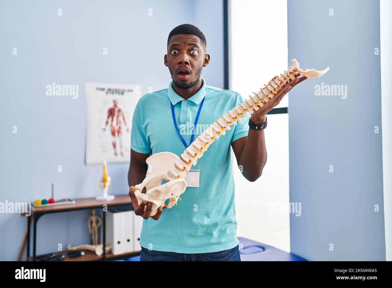 African american man holding anatomical model of spinal column afraid ...