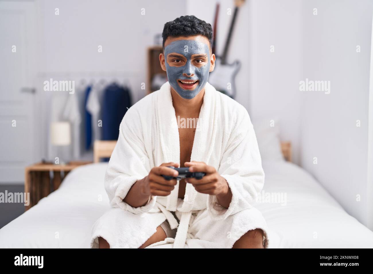 Young hispanic man wearing beauty face mask playing video games smiling ...