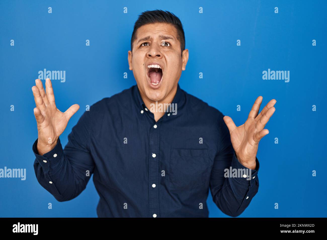 Hispanic young man standing over blue background crazy and mad shouting ...