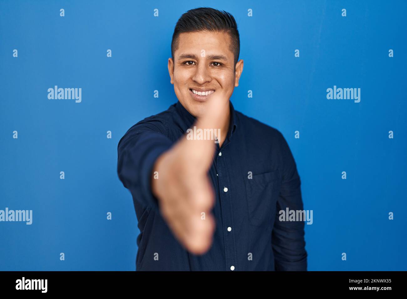 Hispanic young man standing over blue background smiling friendly ...