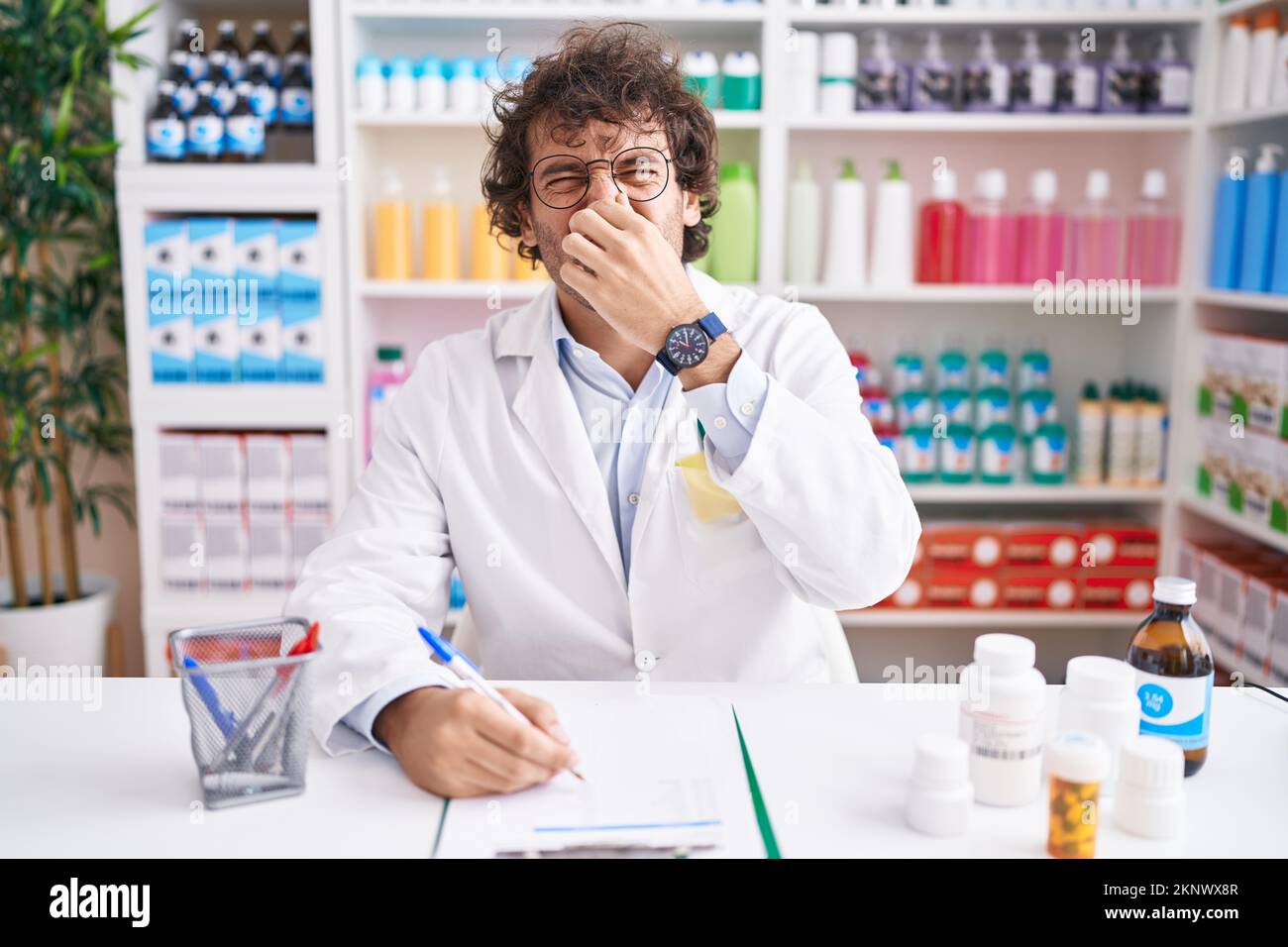 Hispanic young man working at pharmacy drugstore smelling something ...