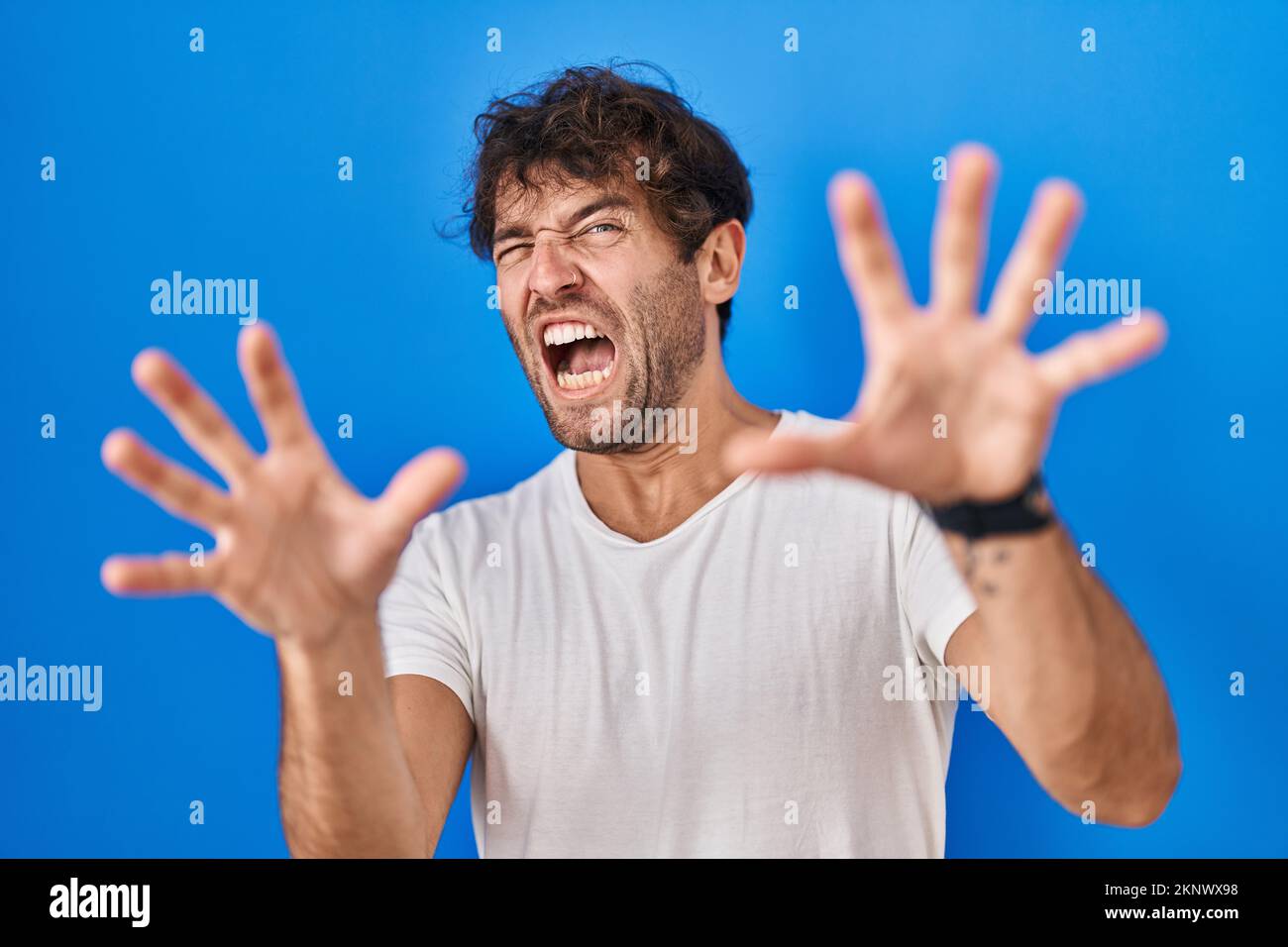 Hispanic young man standing over blue background afraid and terrified ...