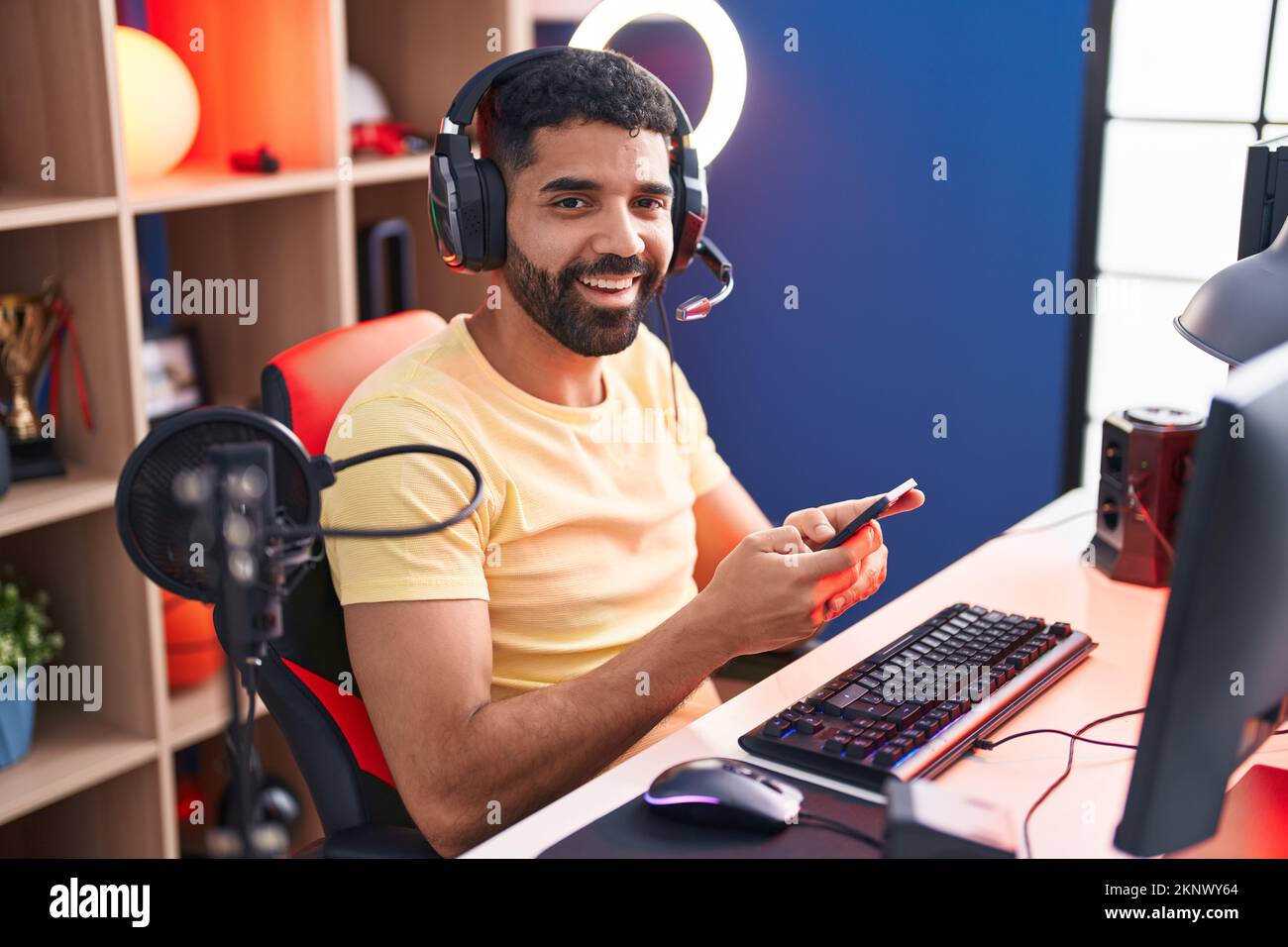 Young arab man streamer using computer and smartphone at gaming room ...