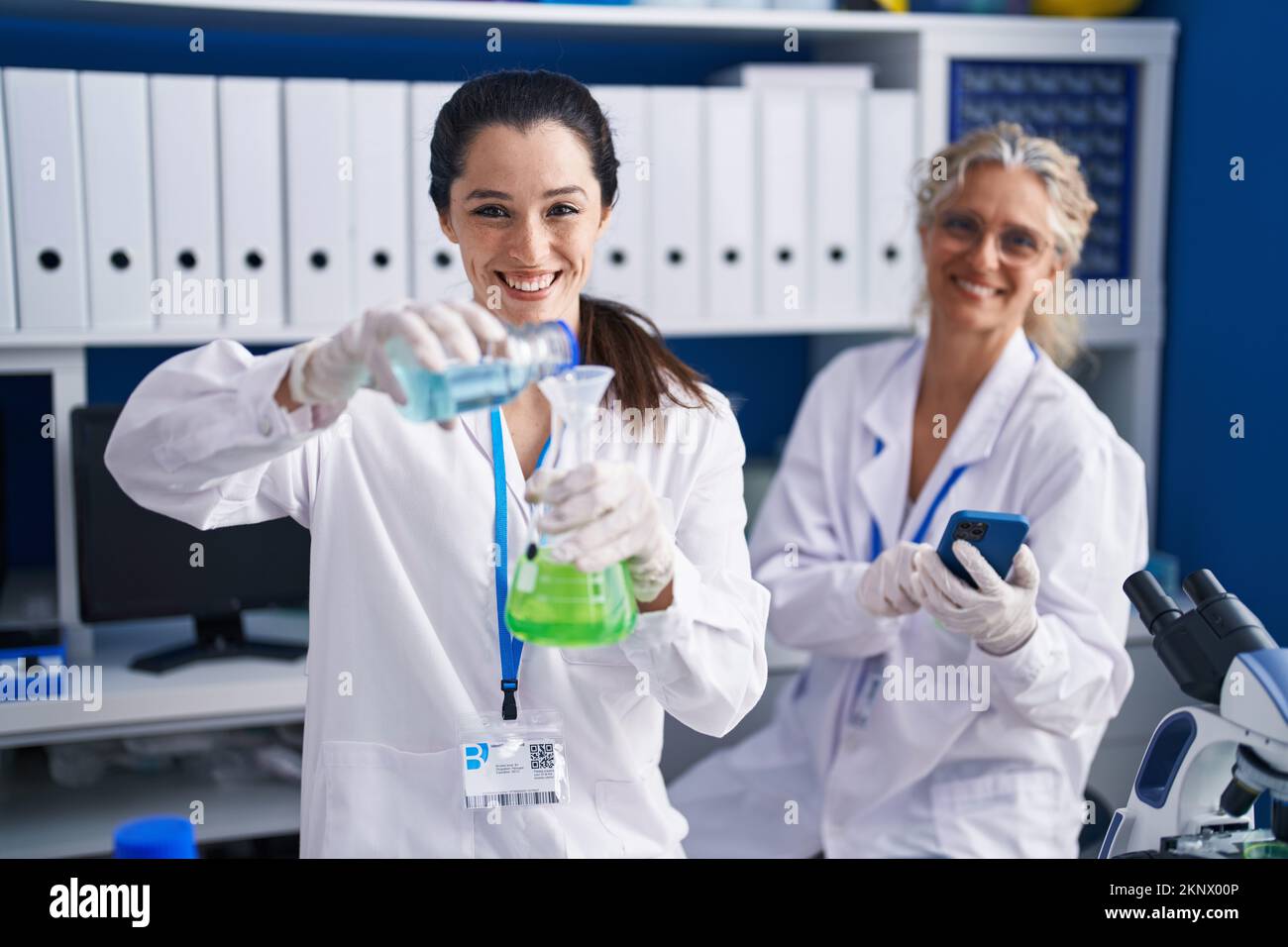Two women scientists using smartphone and measuring liquid at ...