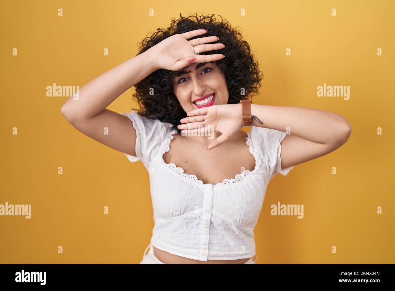 Young brunette woman with curly hair standing over yellow background ...
