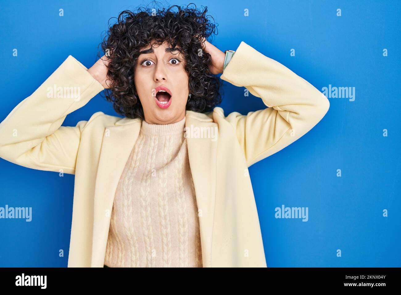 Young brunette woman with curly hair standing over blue background ...