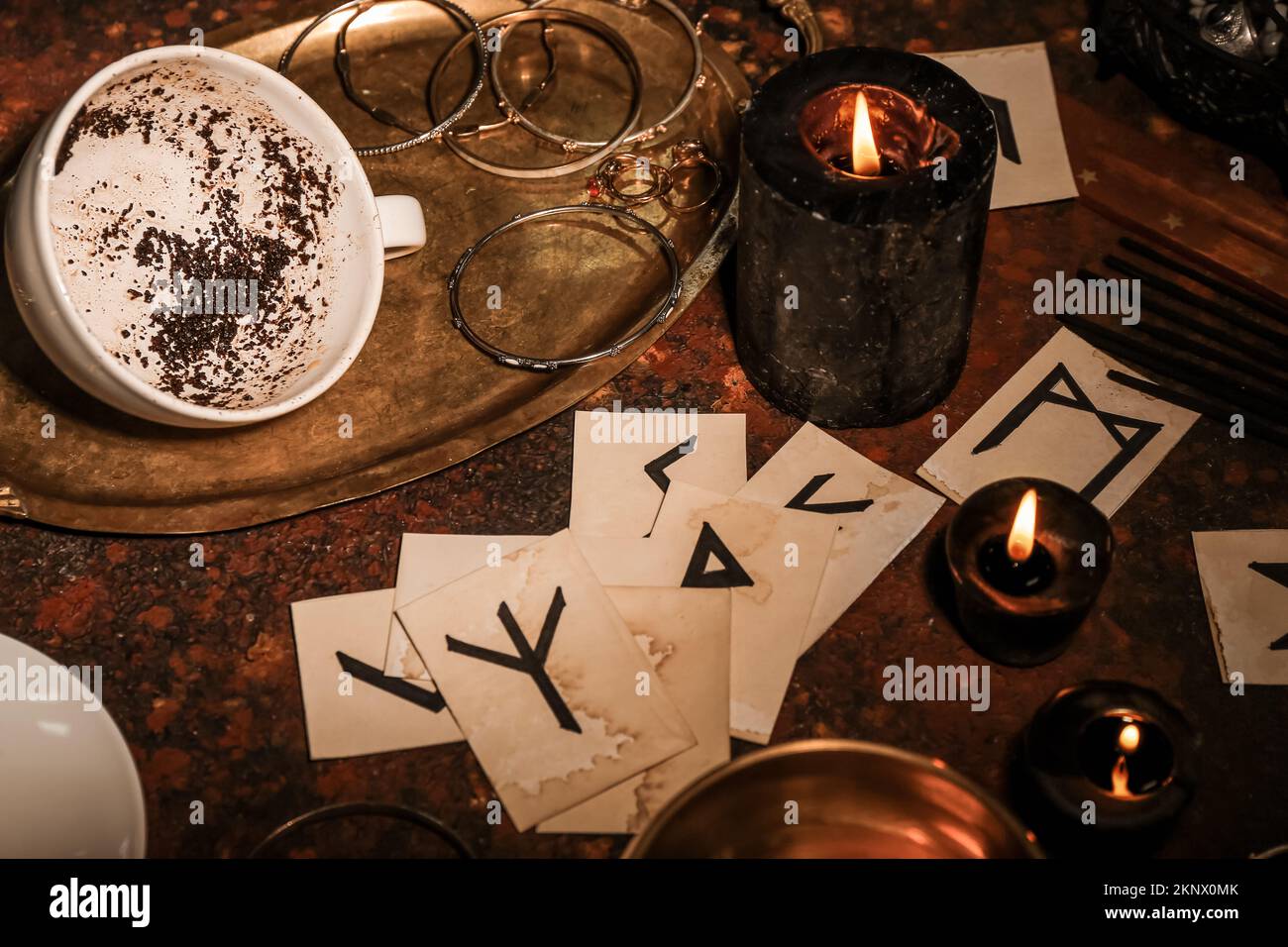 Cup with spent coffee grounds and runes for fortune telling on table ...