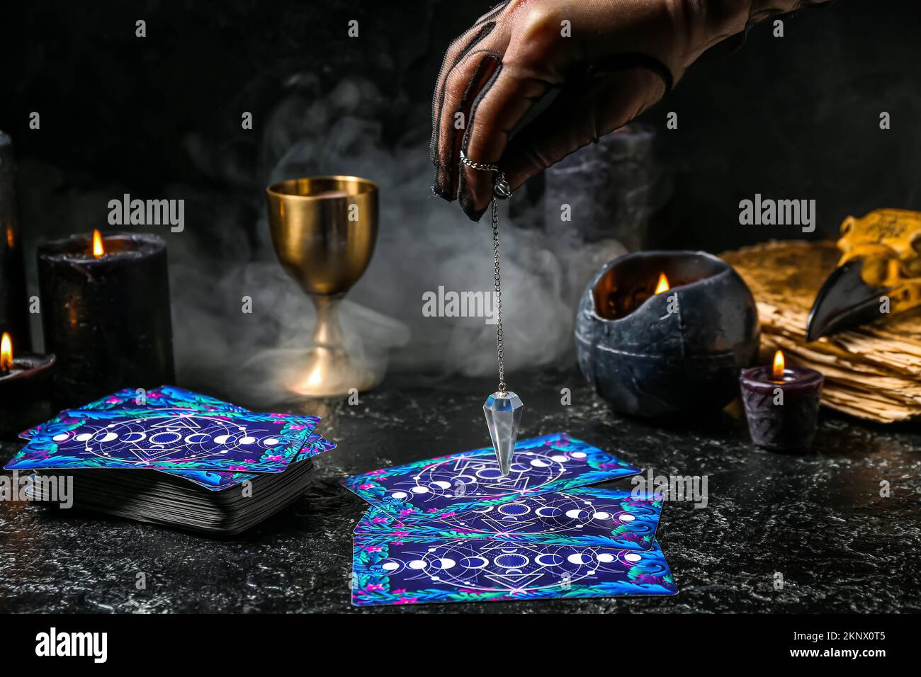 Fortune teller using pendulum and tarot cards to read future on dark ...