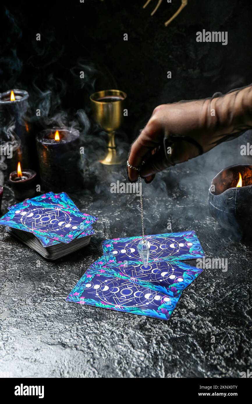 Fortune teller using pendulum and tarot cards to read future on dark ...