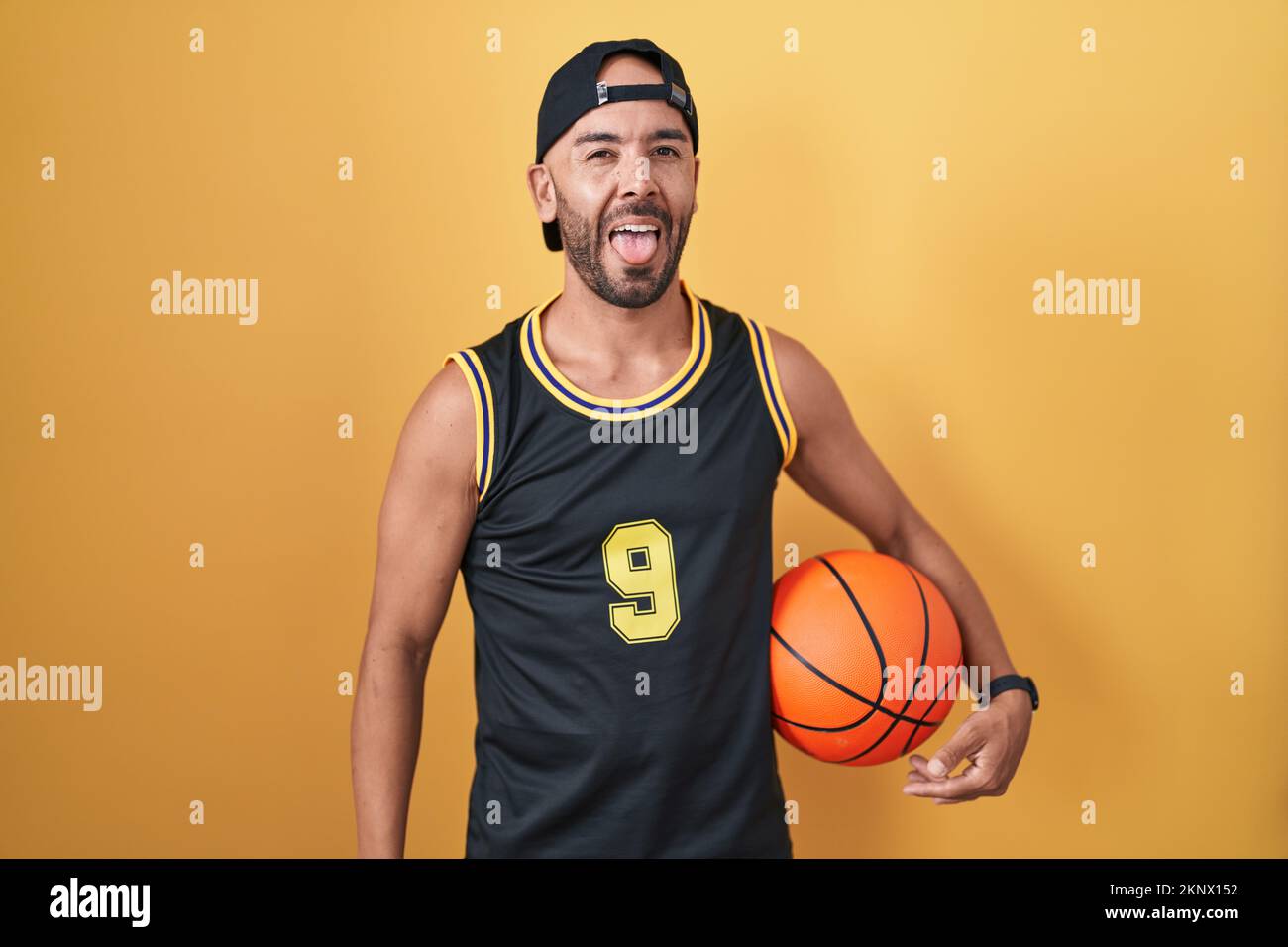 Middle age bald man holding basketball ball over yellow background ...