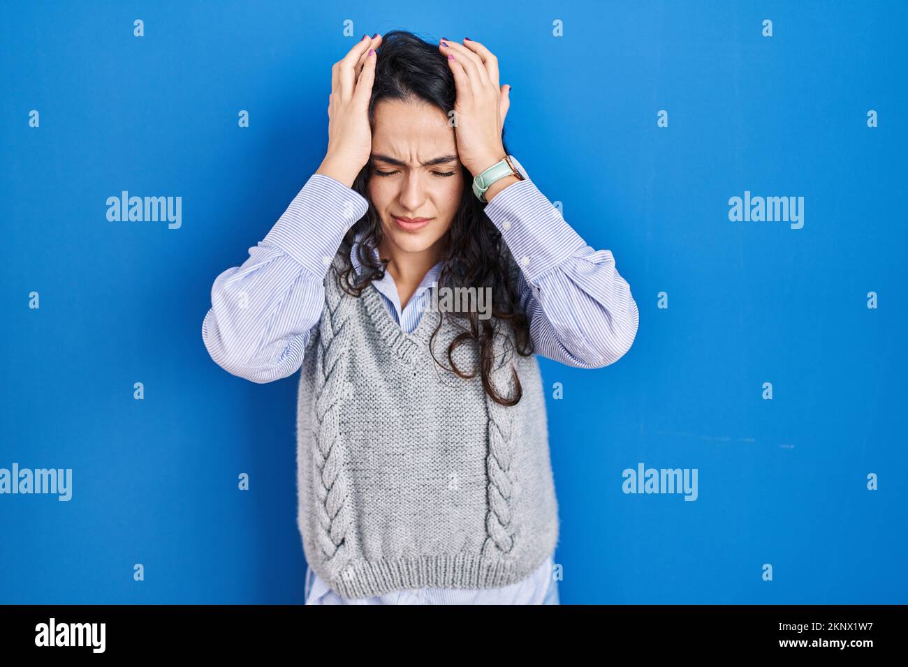 Young brunette woman standing over blue background suffering from ...