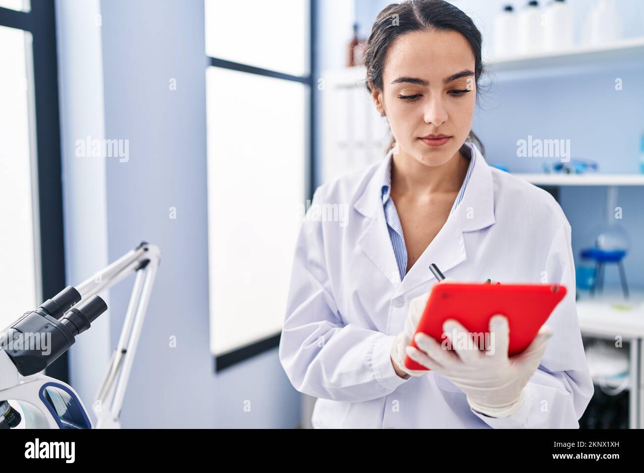 Young hispanic woman wearing scientist uniform using touchpad at ...