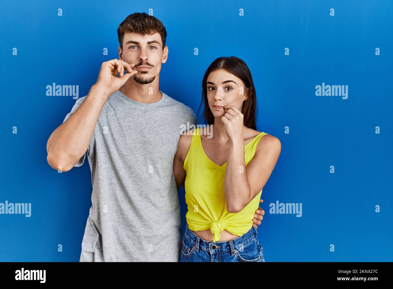 Young hispanic couple standing together over blue background mouth and ...