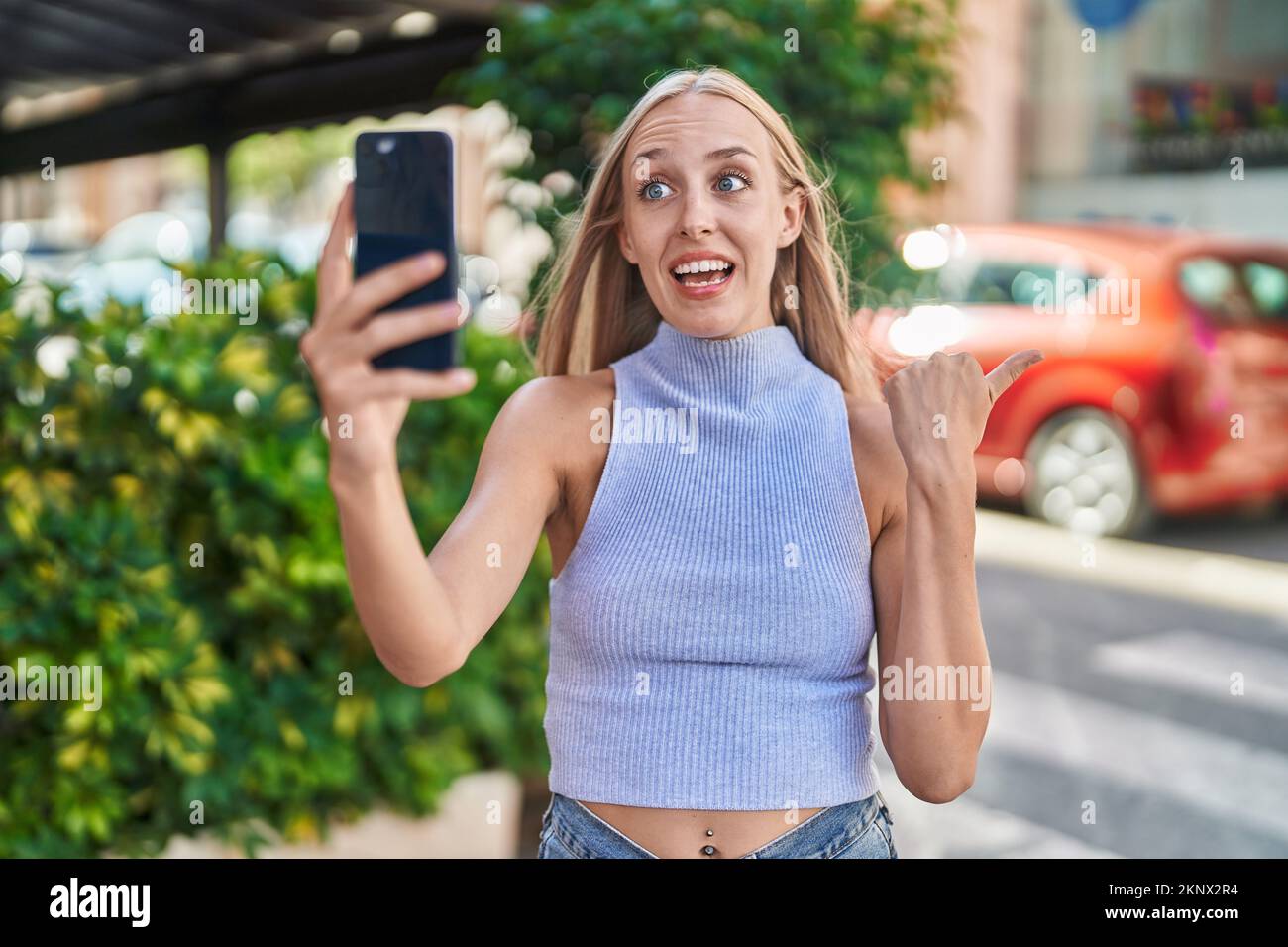 Young caucasian woman doing video call with smartphone pointing thumb ...