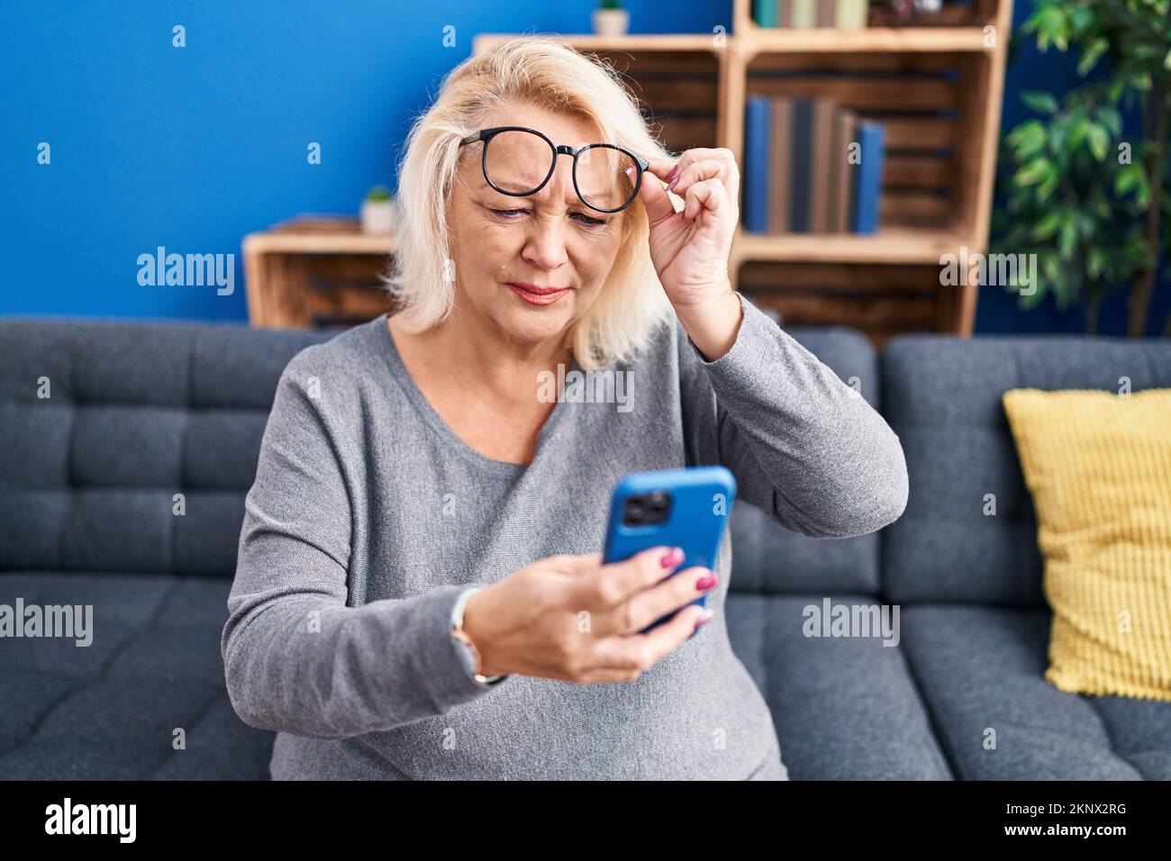 Middle age blonde woman using smartphone sitting on sofa at home Stock ...