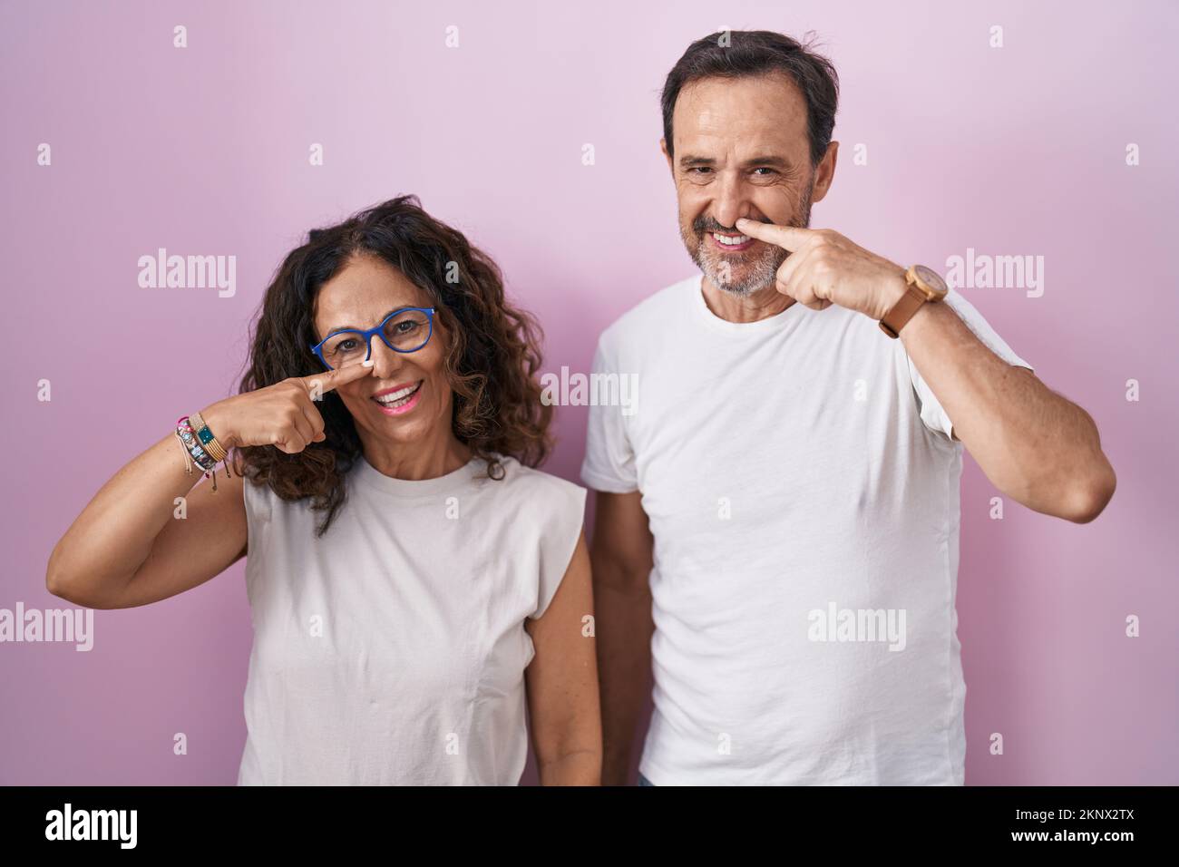 Middle age hispanic couple together over pink background pointing with ...