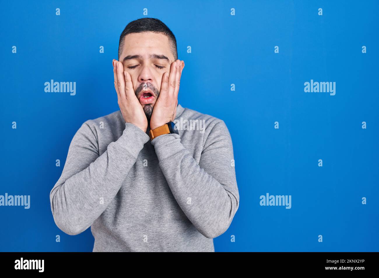 Hispanic man standing over blue background tired hands covering face ...