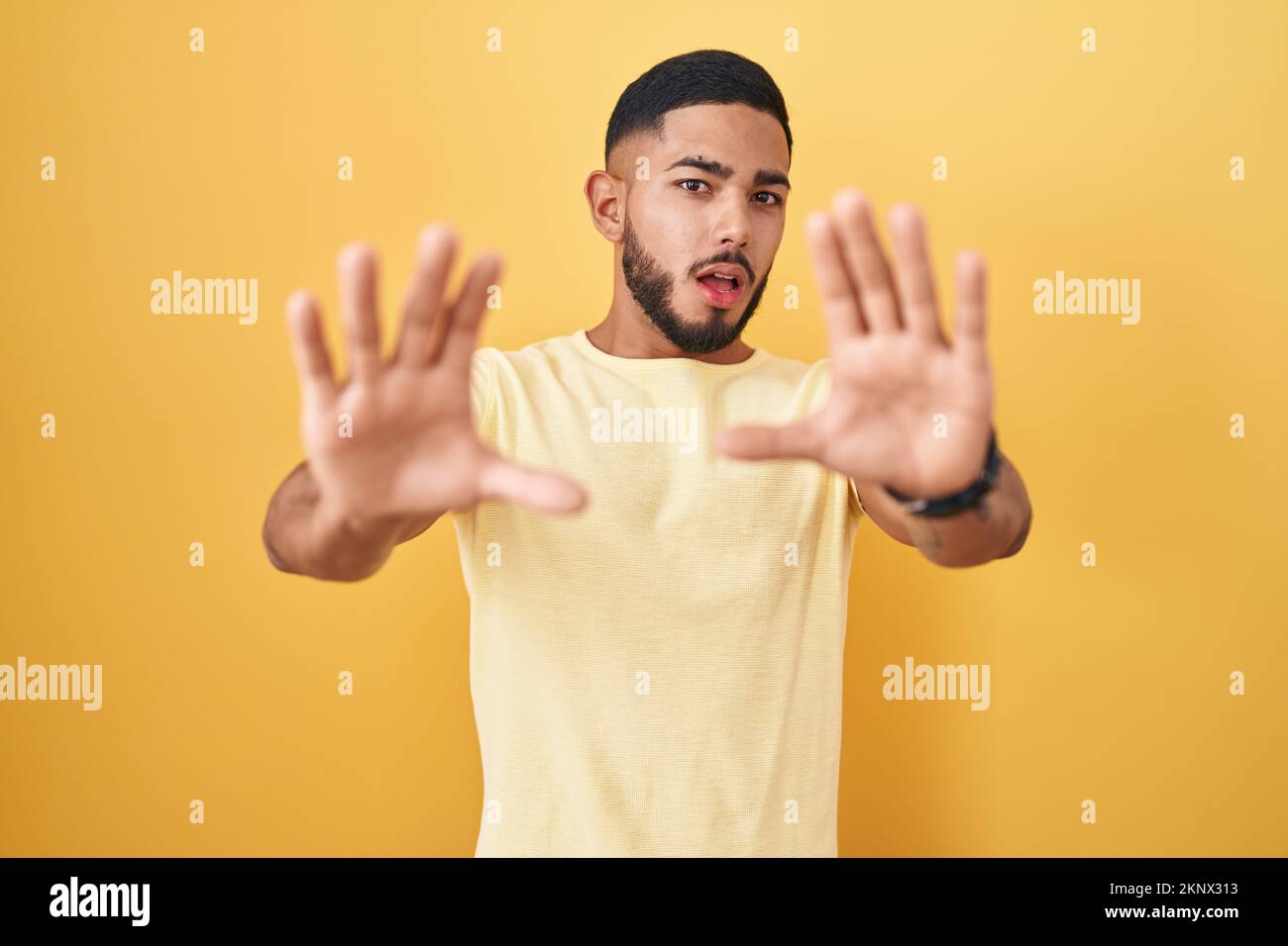 Young hispanic man standing over yellow background afraid and terrified ...