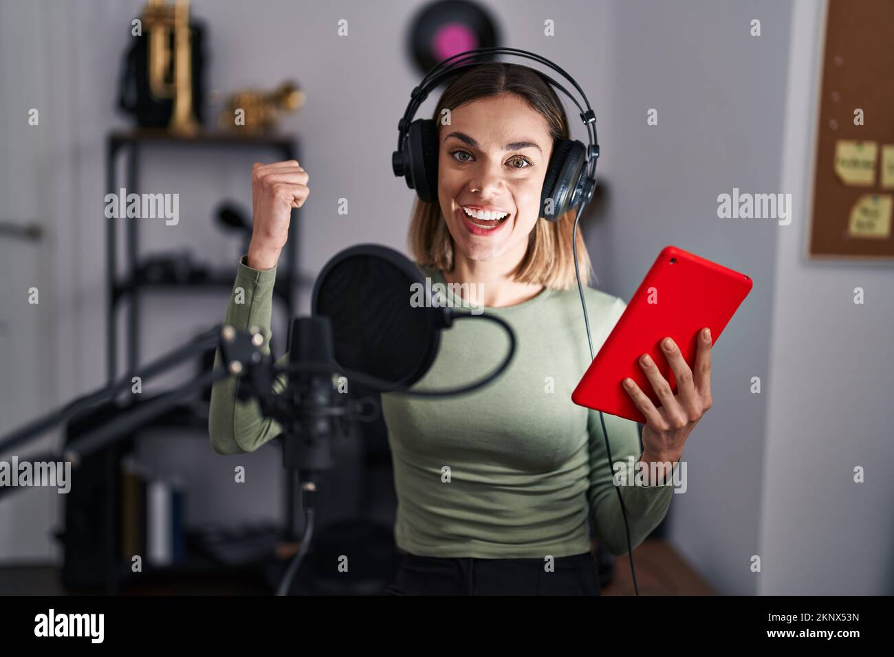 Hispanic woman singing song using microphone and tablet pointing thumb ...