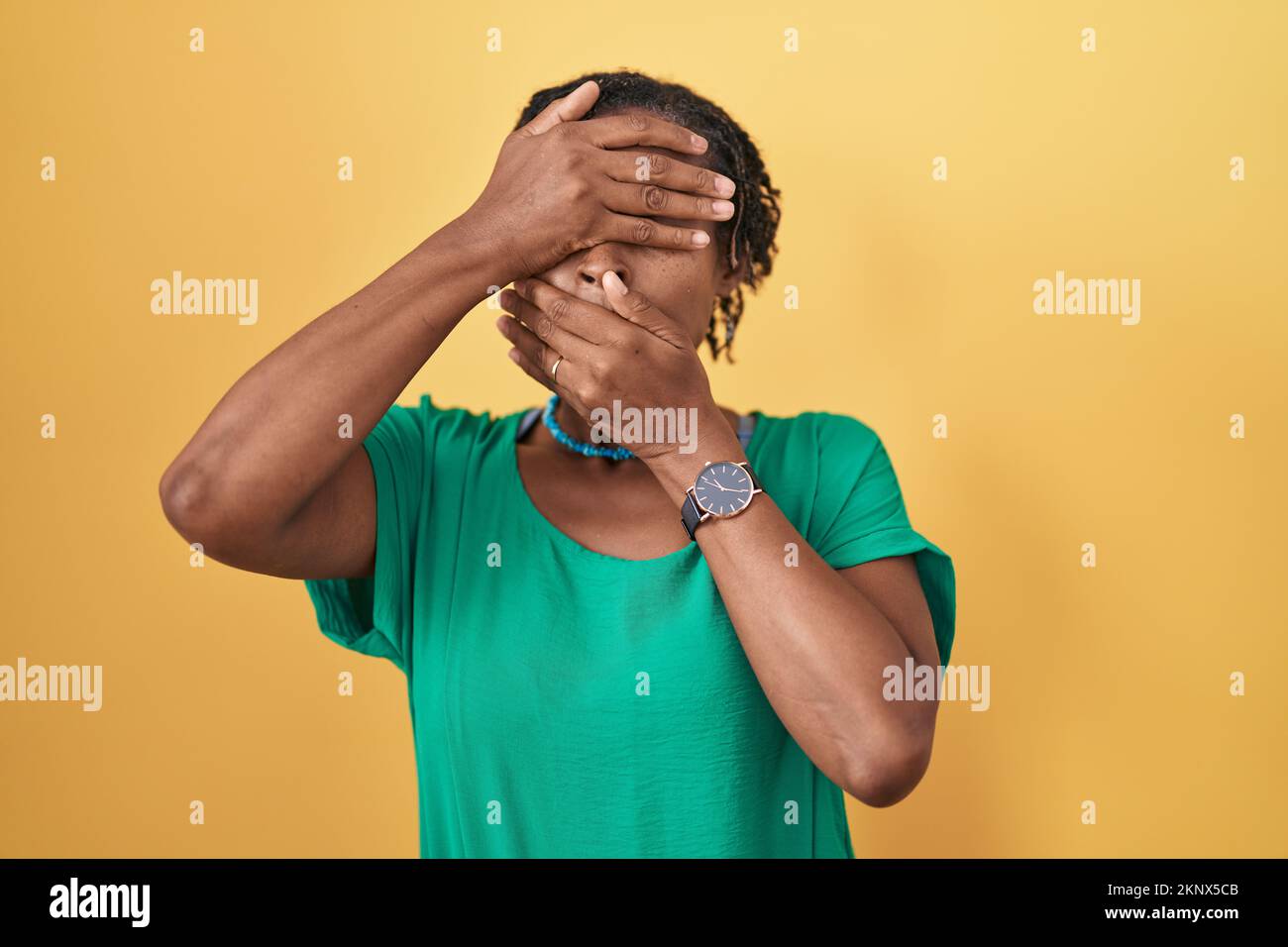 African woman with dreadlocks standing over yellow background covering ...
