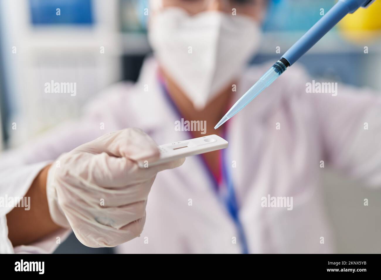 Young beautiful hispanic woman scientist pouring liquid to antigen test ...