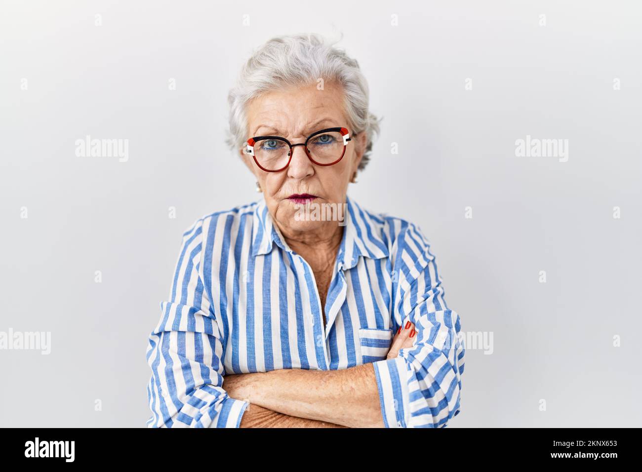 Senior woman with grey hair standing over white background skeptic and ...