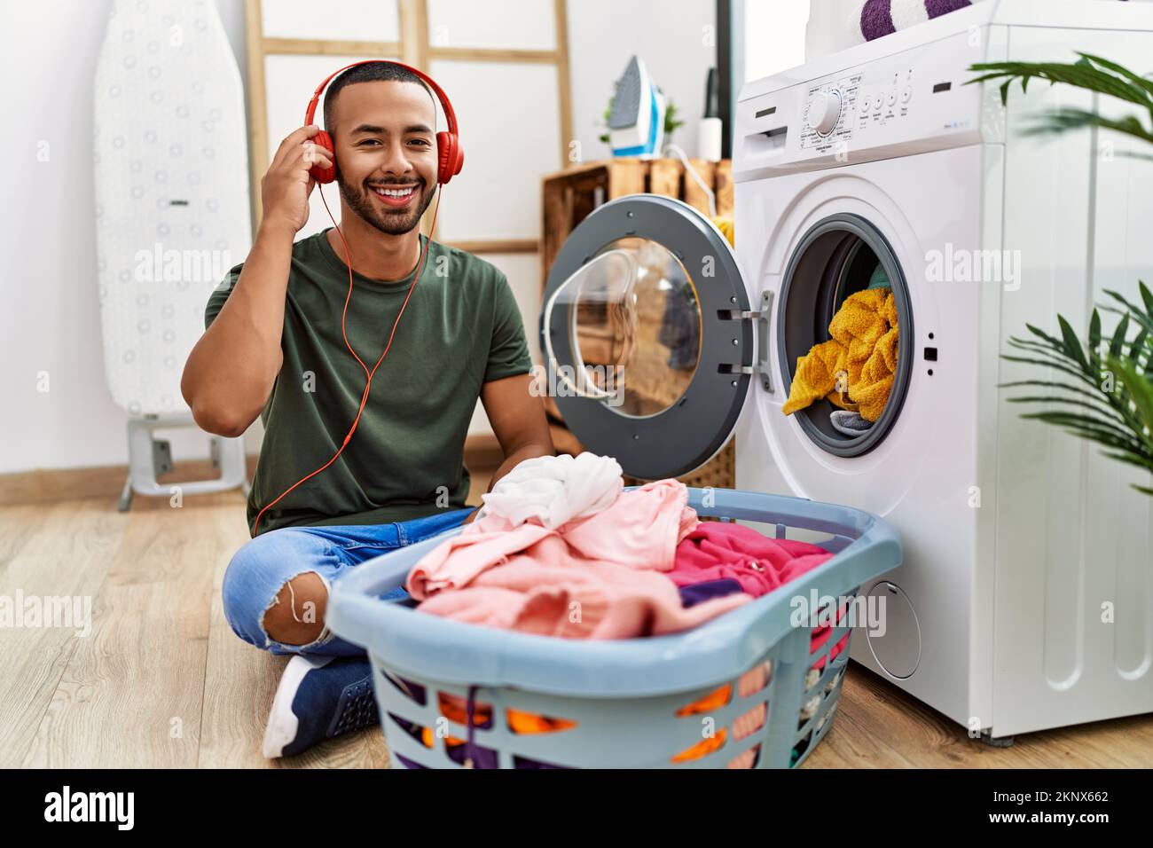 Young hispanic man listening to music using washing machine at laundry ...