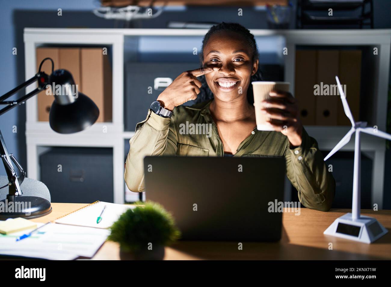 African woman working using computer laptop at night pointing with hand ...