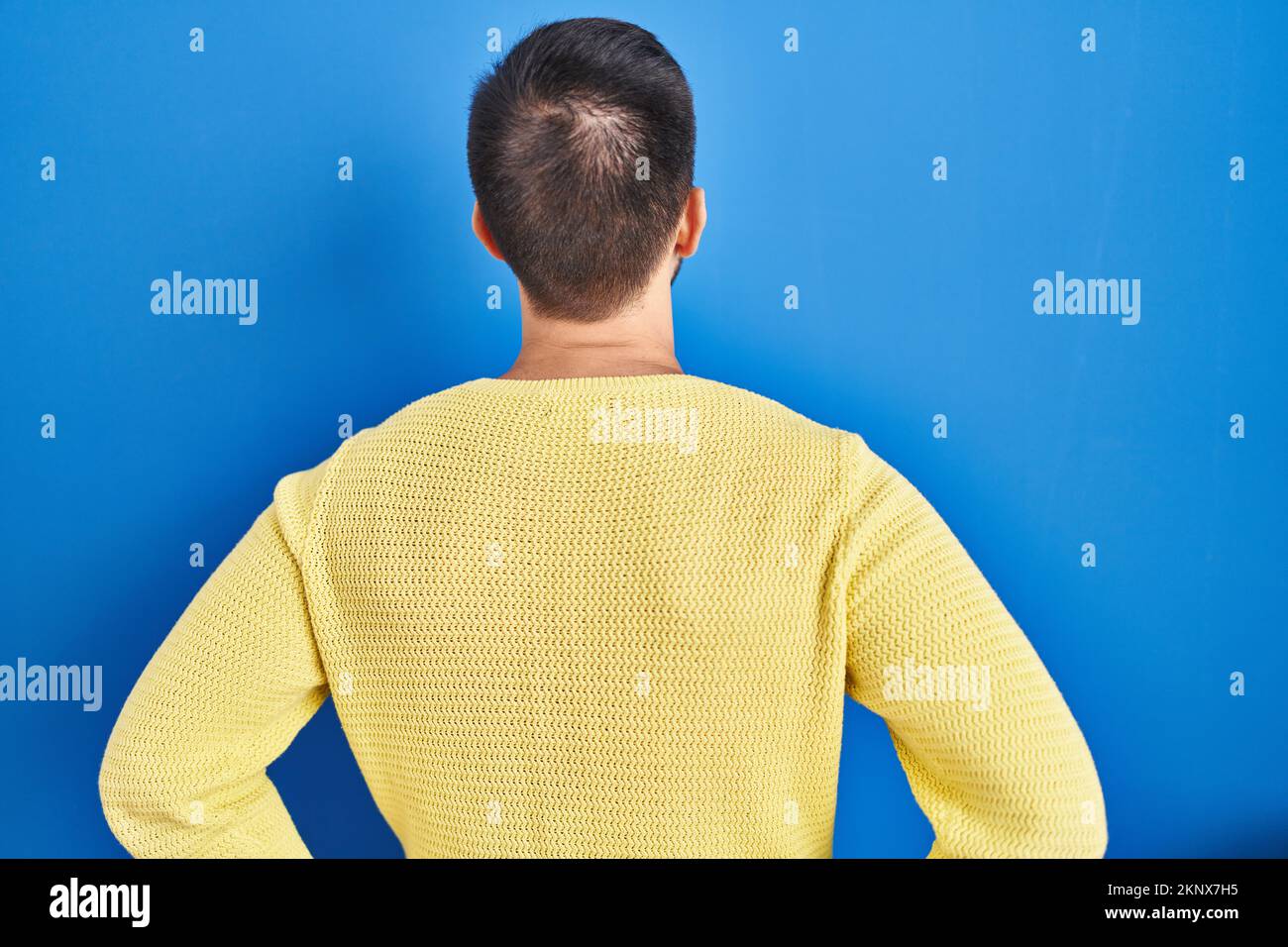 Hispanic man standing over blue background standing backwards looking ...