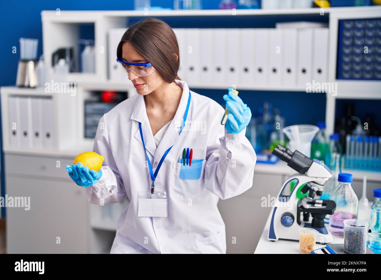 Young beautiful hispanic woman scientist holding lemon and test tube at ...