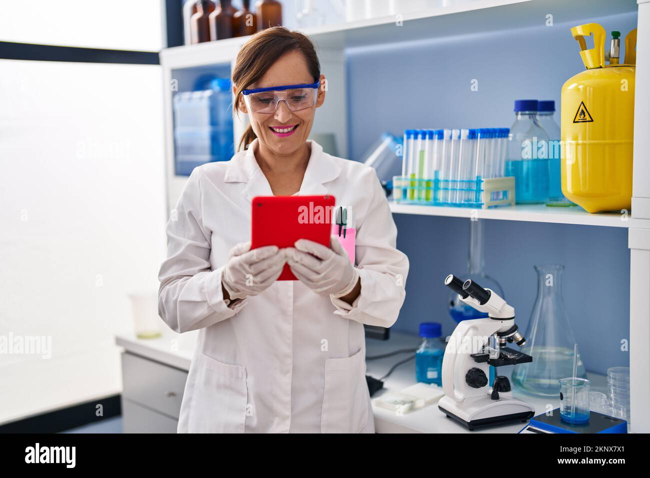 Middle age woman wearing scientist uniform using touchpad at laboratory ...