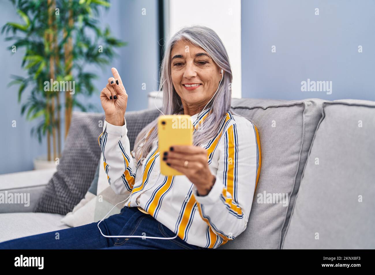 Middle age woman with grey hair using smartphone sitting on the sofa ...