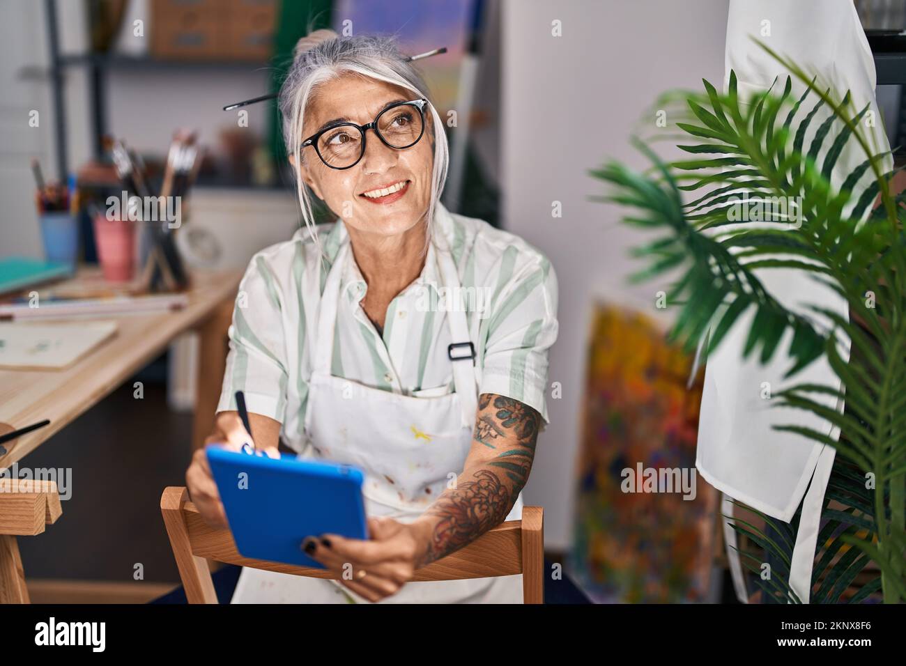 Middle age grey-haired woman artist smiling confident using touchpad at ...