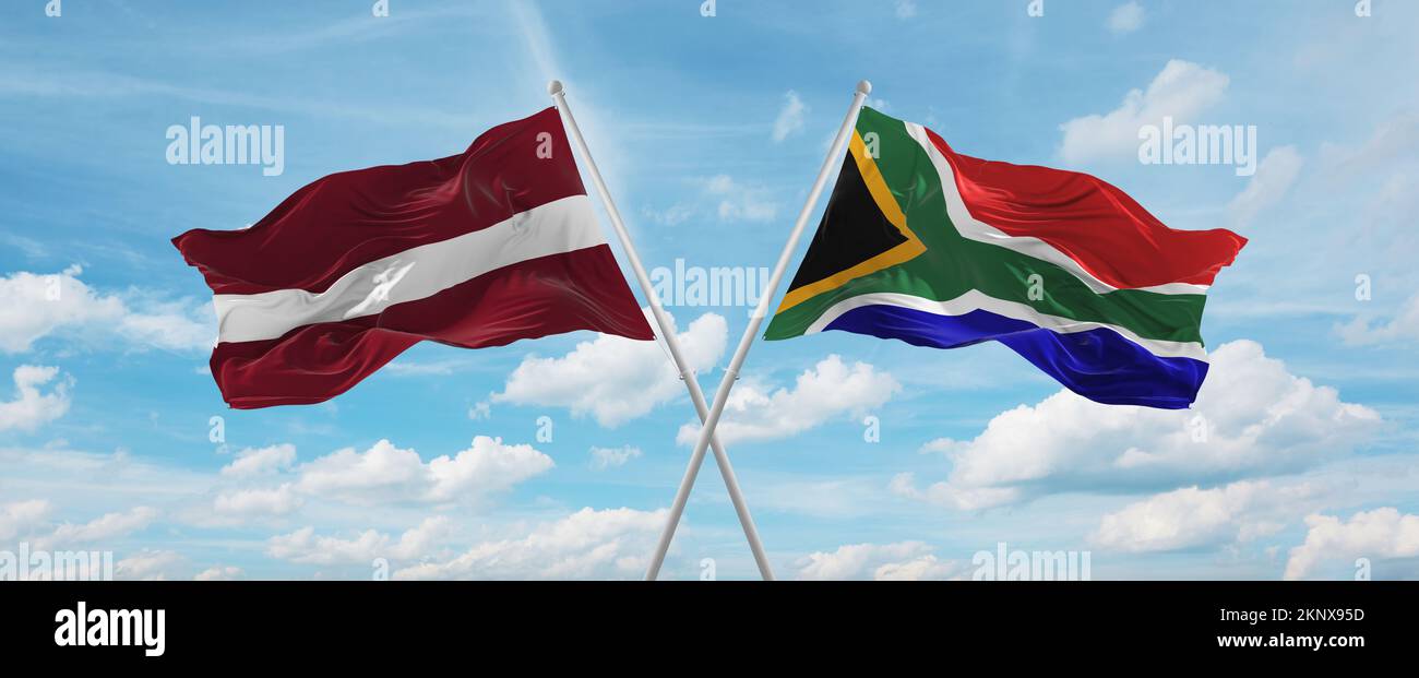 two crossed flags South Africa and Latvia waving in wind at cloudy sky ...