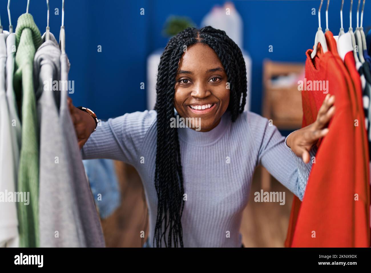 African american woman searching clothes on clothing rack smiling with ...