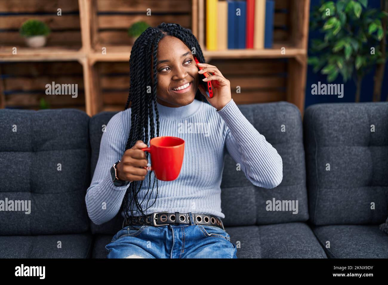 African american woman talking on smartphone drinking coffee at home ...