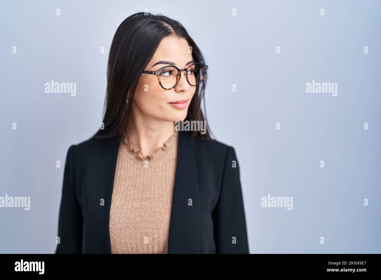 Young brunette woman standing over blue background looking to side ...