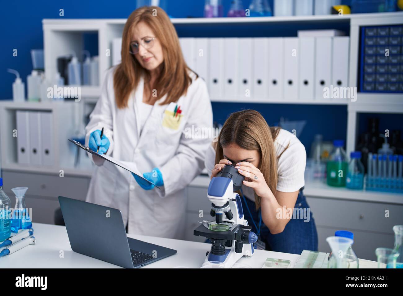Mother and daughter scientists writing on document using microscope at ...