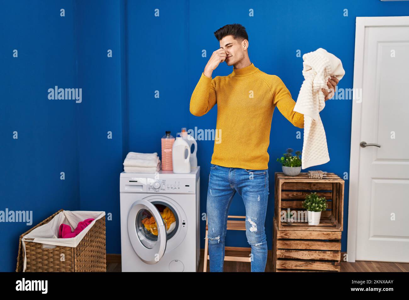 Young hispanic man washing clothes smelling dirty clothes at laundry ...