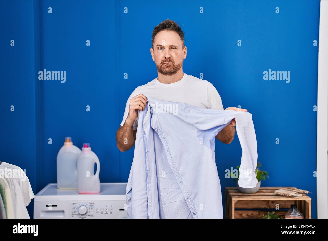 Middle age caucasian man holding shirt with sweat skeptic and nervous ...